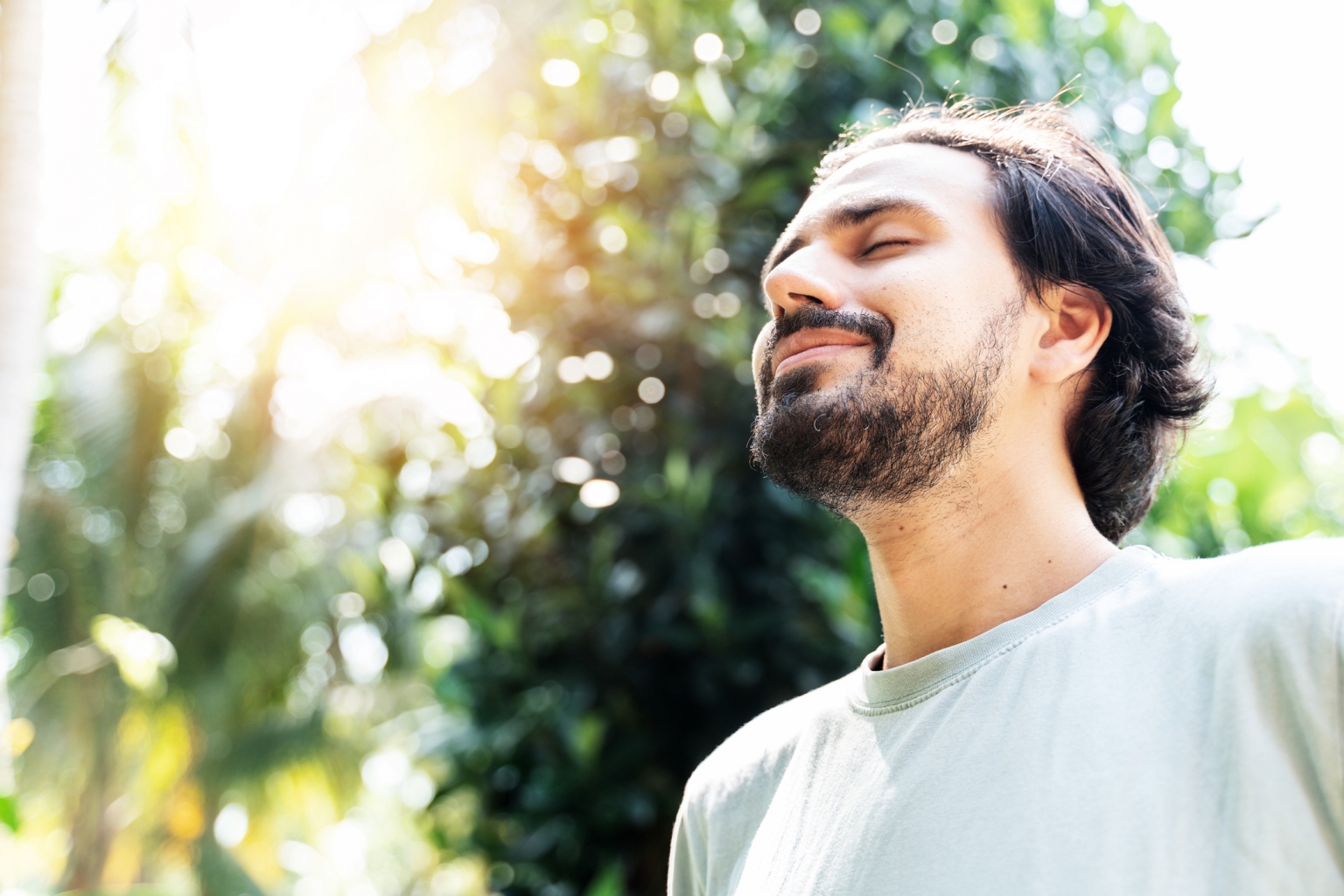 A bearded man is meditating outdoor in the park with face raised up to ...